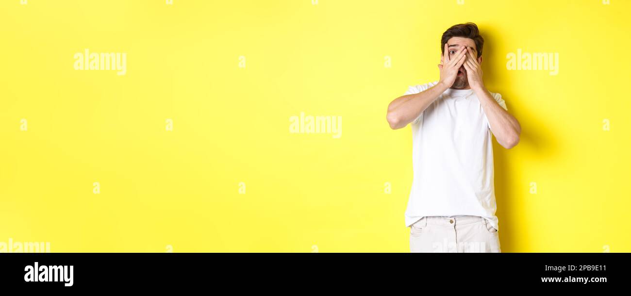 Embarrassed guy shut eyes but peeking through fingers at something ...