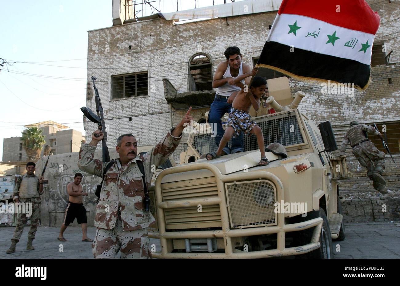 Iraqi soldier shoots in the air as people, waving Iraqi flag, celebrate ...