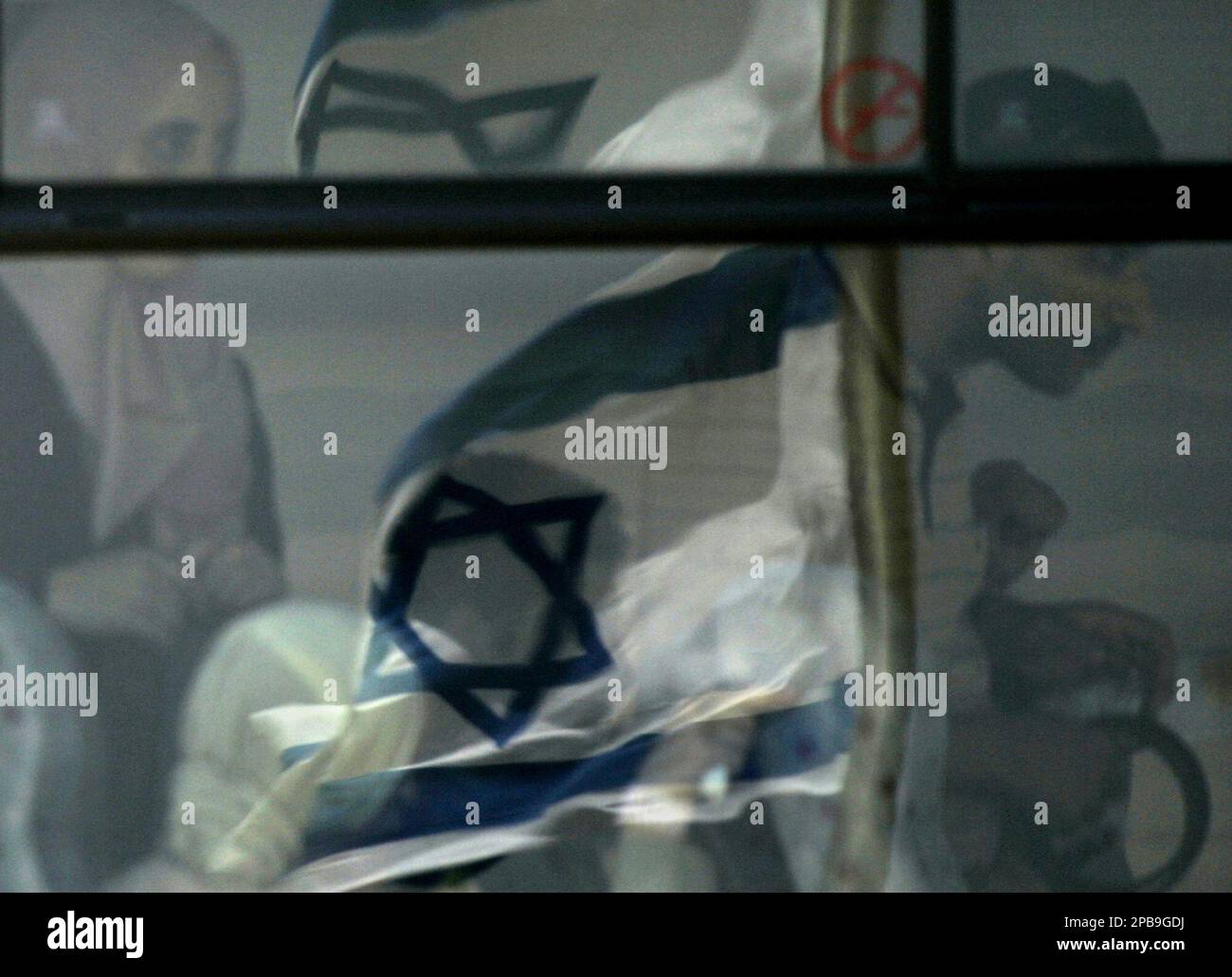 An Israeli flag is reflected in a window as Palestinians wait on a bus ...