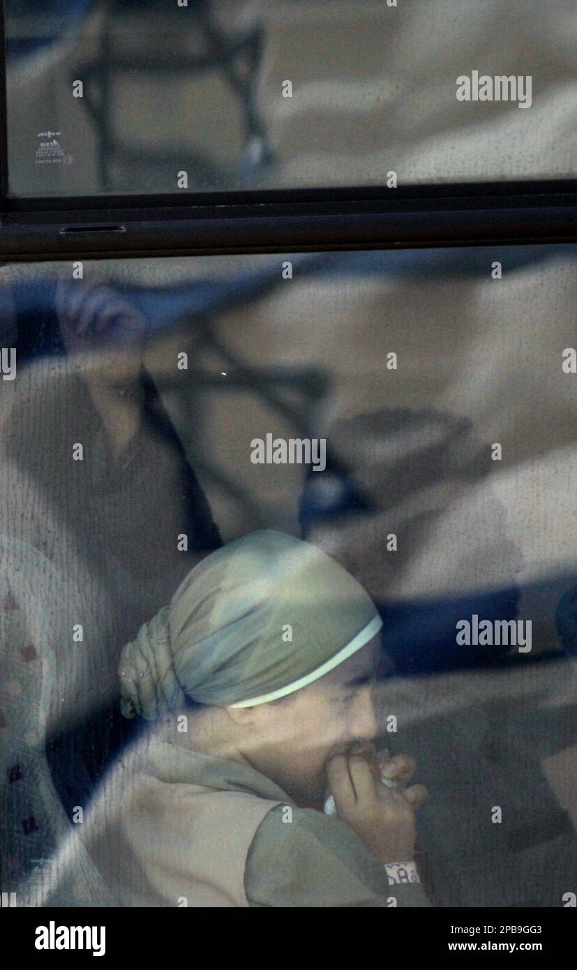 An Israeli flag is reflected in a window as a Palestinian woman sits on ...