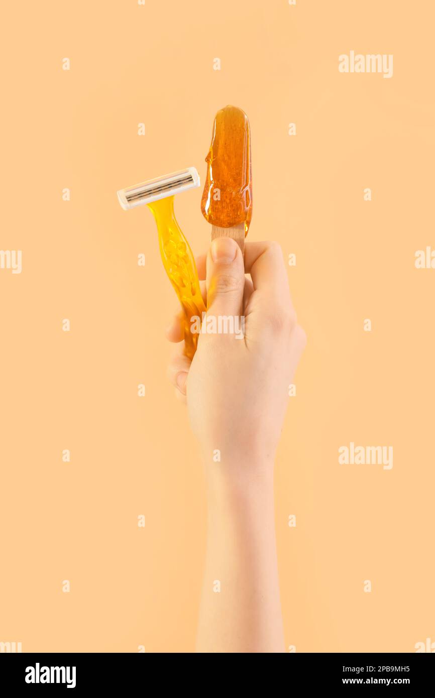 Female hand holding spatula with sugaring paste and razor on beige ...