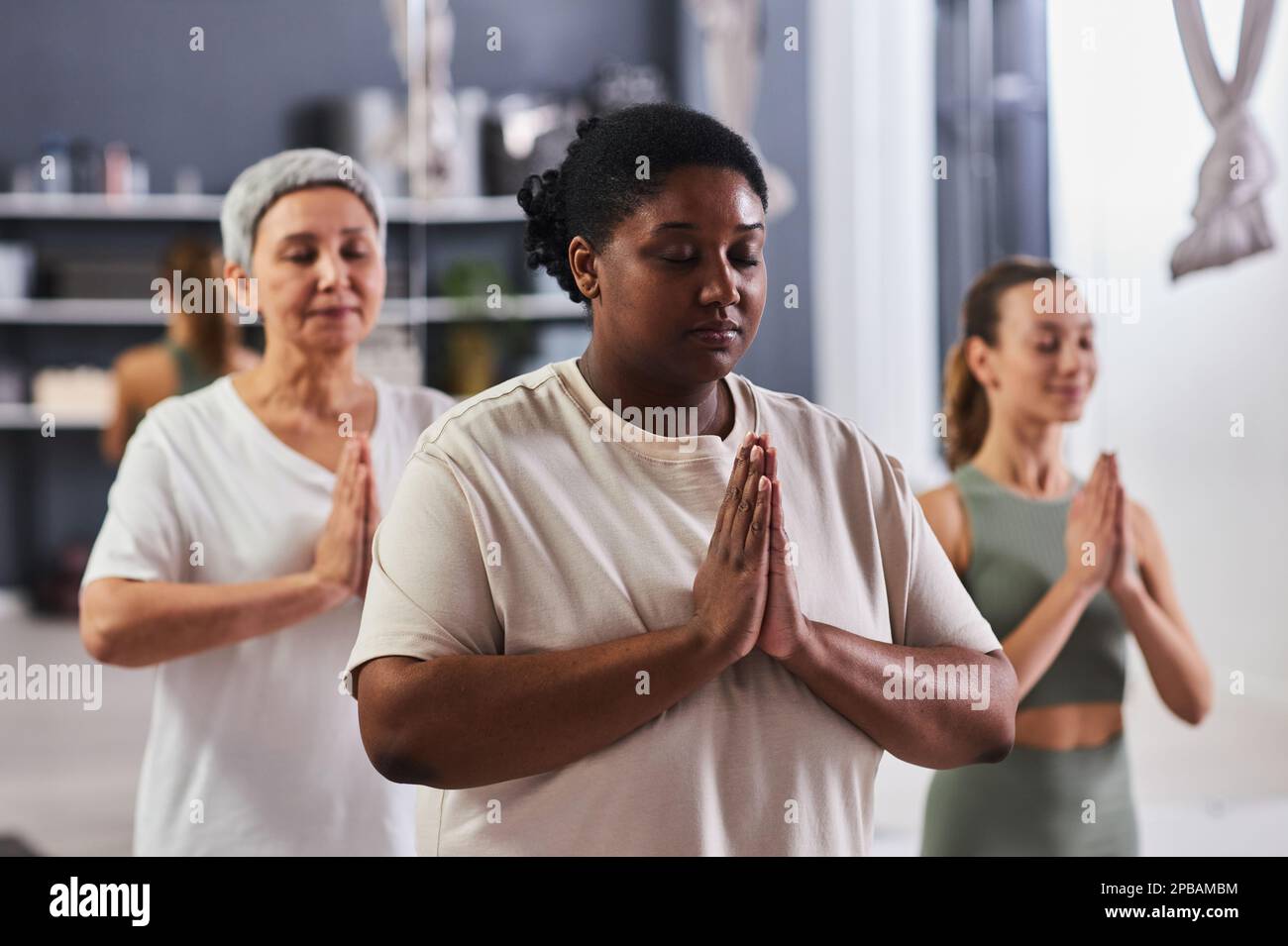 Group of women standing with their eyes closed and doing yoga in health ...