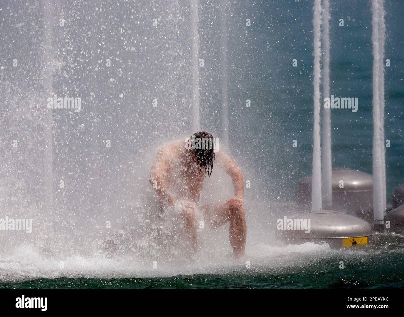 A young man refreshes himself under the jet of a water fountain on the ...