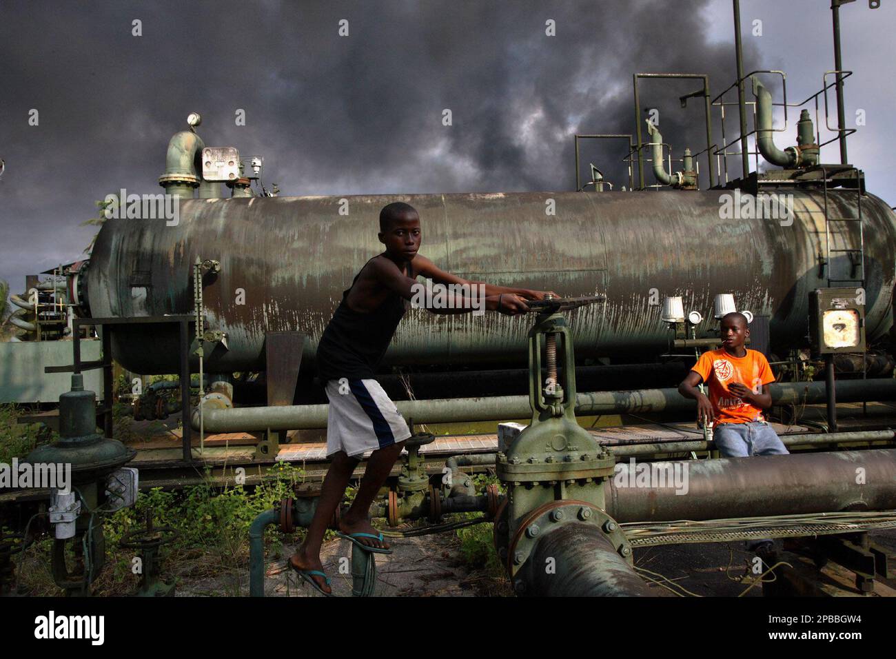 Children play on an abandoned Shell oil flow station while smoke from a ...