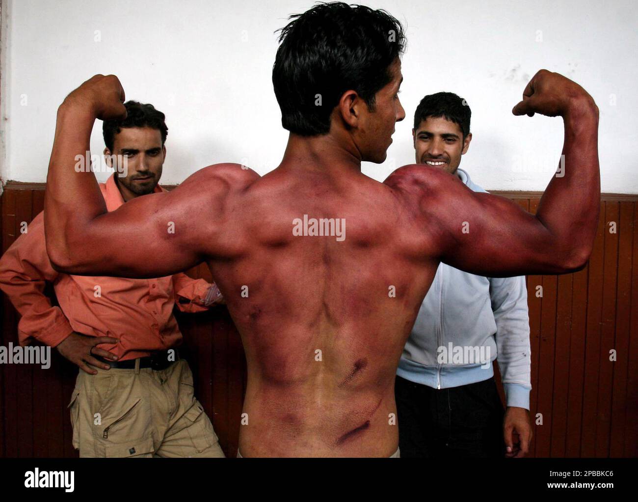 People look on as a Kashmiri body builder displays his muscles as he ...