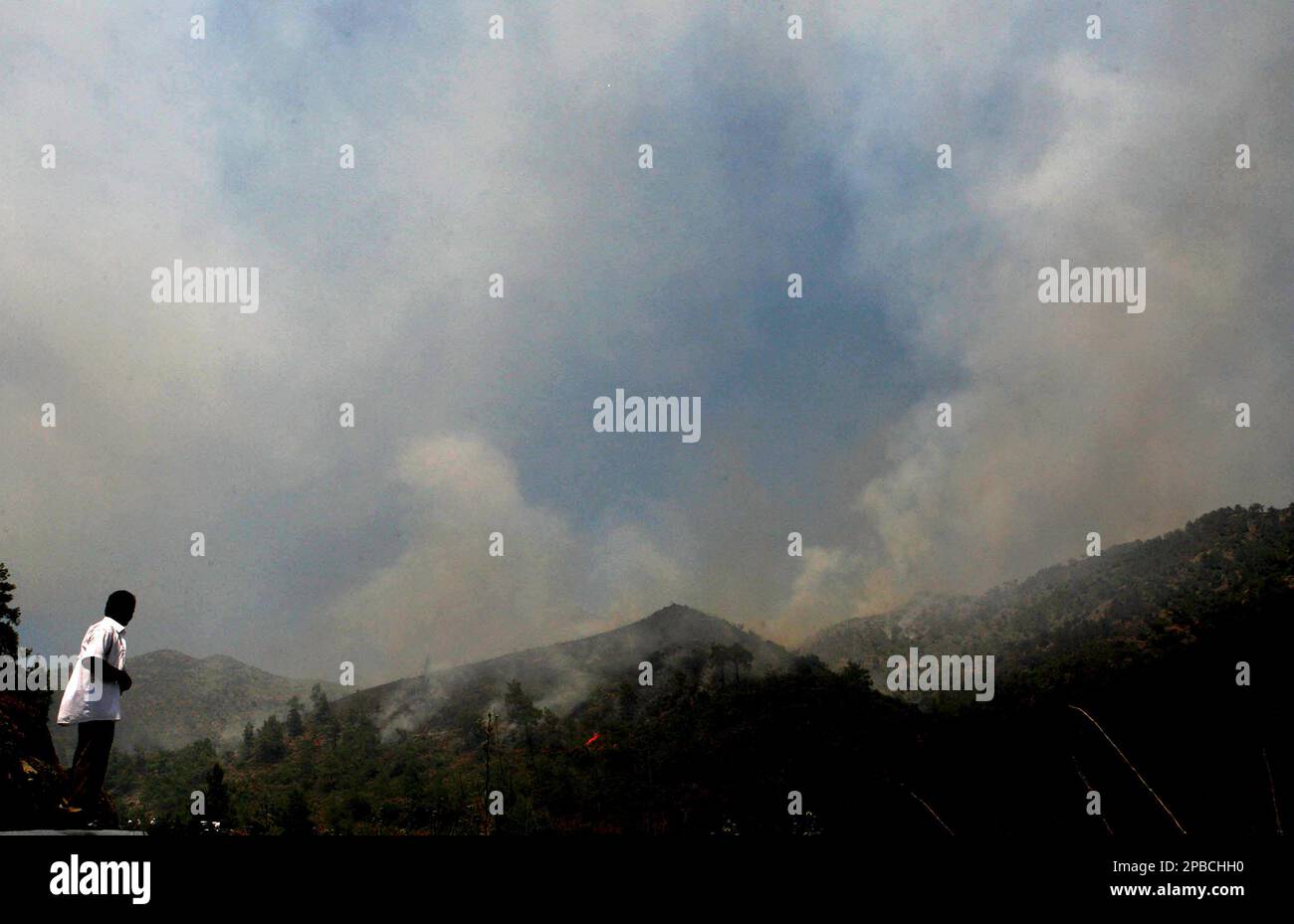 A Cypriot man watches the smoke rise from a fire on the mountains in ...