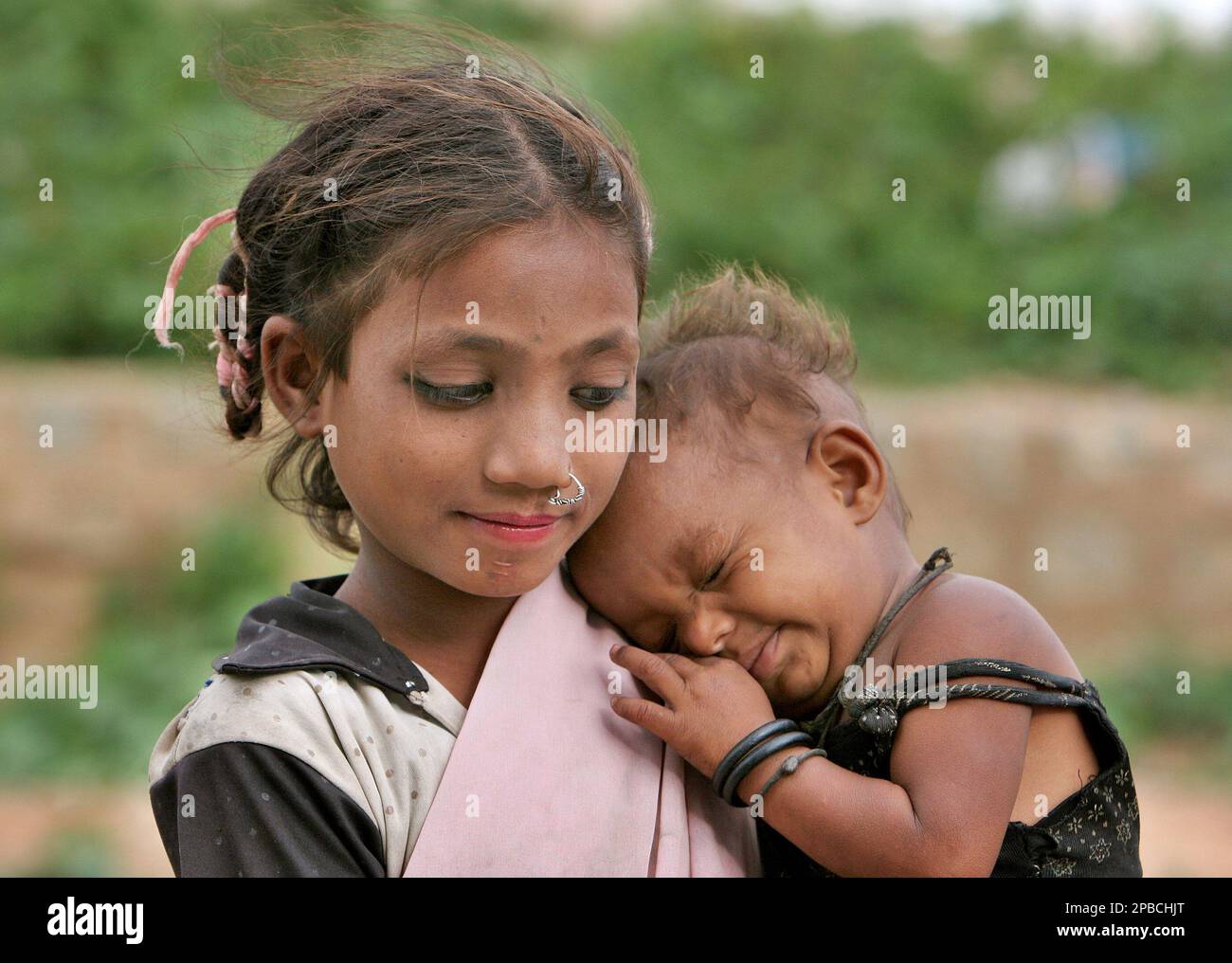 A slum dweller Madhu, 8, holds her one-year-old sister Simran, eyes ...