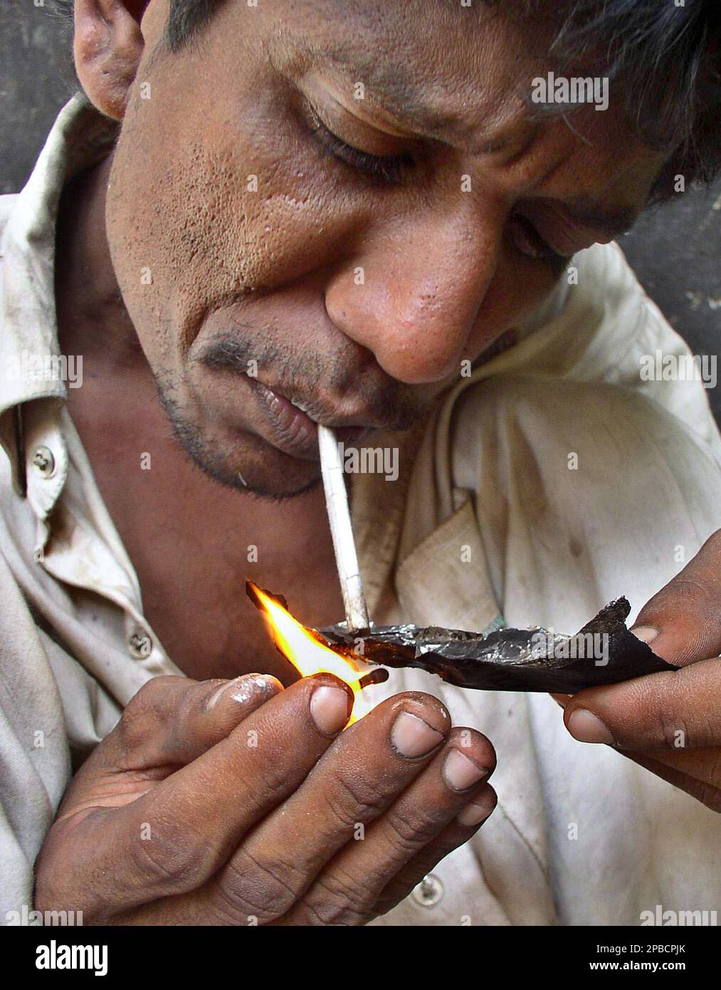 A Pakistani drug addict smokes heroin at a slum area in Hyderabad ...