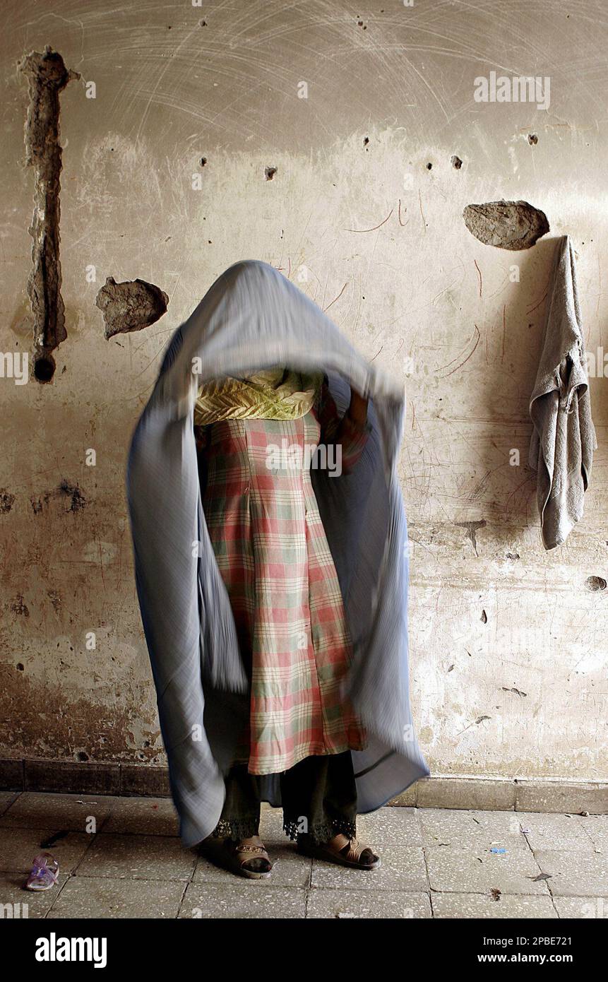An Afghan woman puts on her burqa before leaving home in Kabul ...