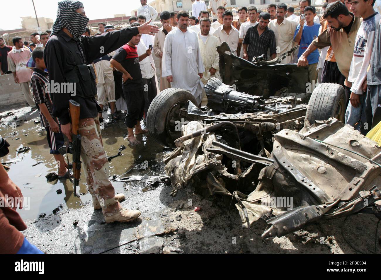 A gunman and Iraqi civilians inspect the damage after a parked minibus ...