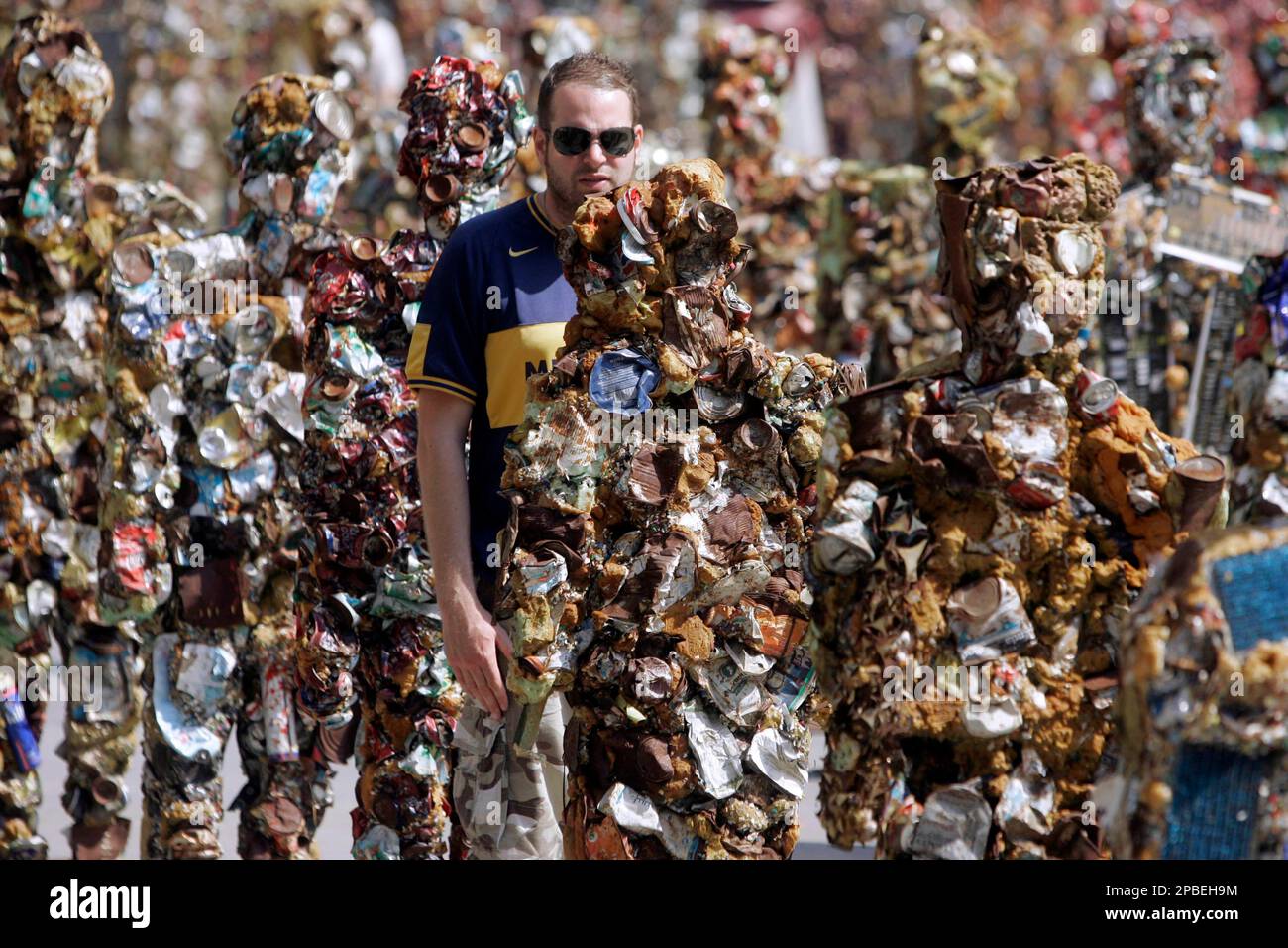A man stands between rows of life-sized mannequins made of waste ...