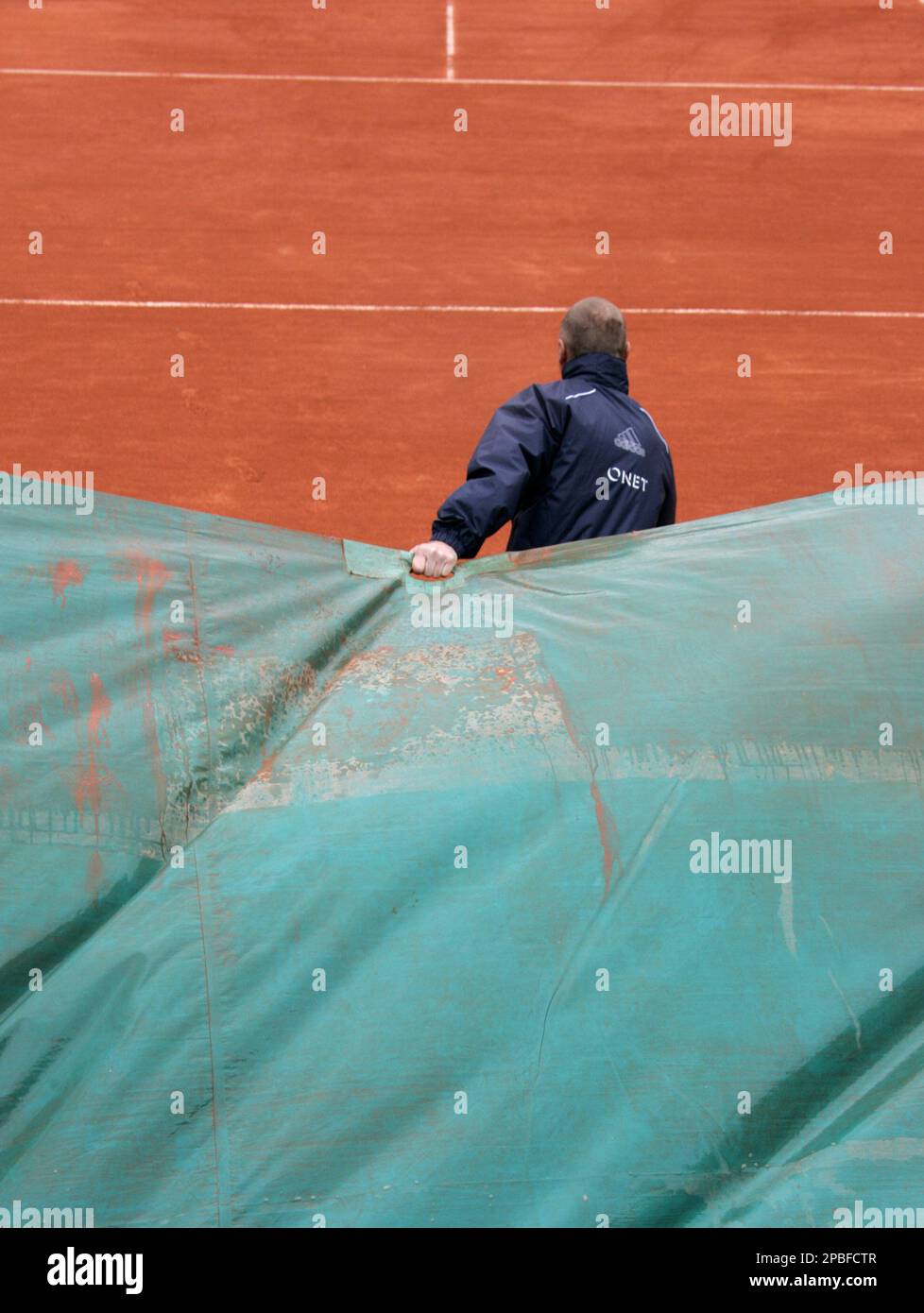 A stadium employee pulls a rain protection cover over center court ...