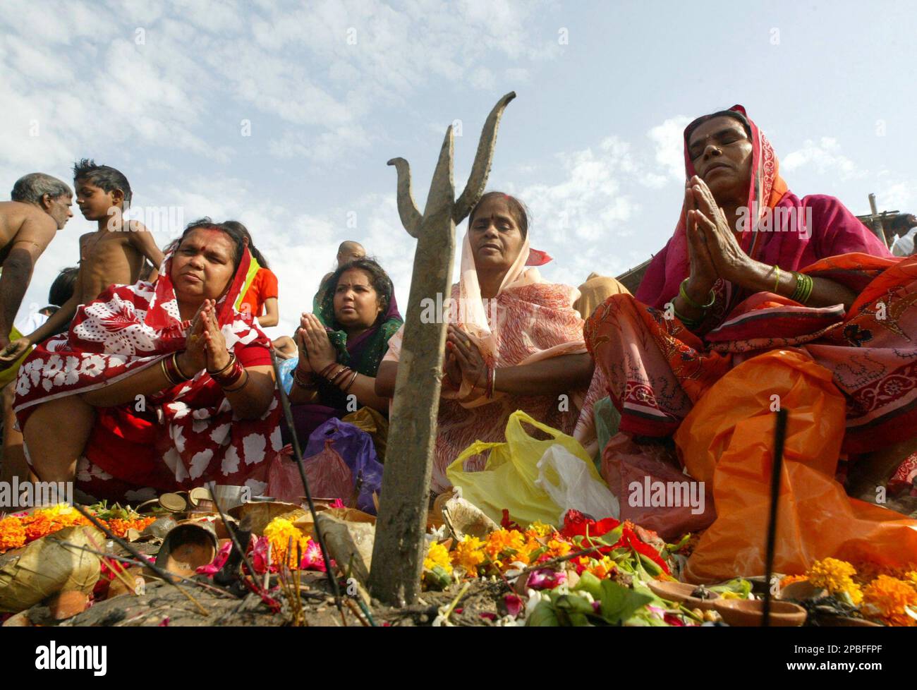Hindu women offer prayers in front of a trident, a weapon associated ...