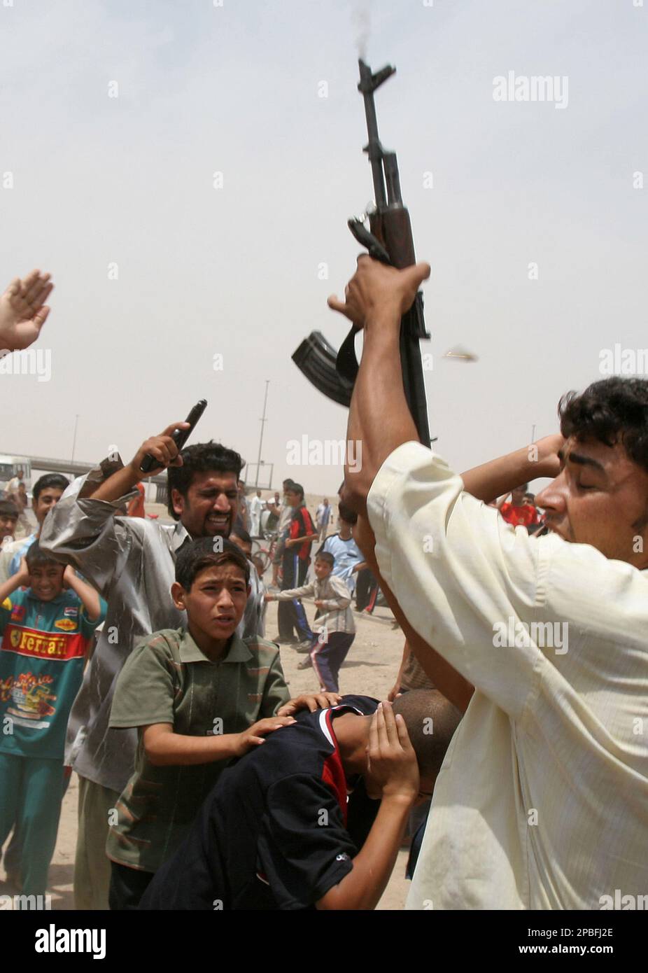 An Iraqi man shoot in the air with his rifle next to a burning sports ...
