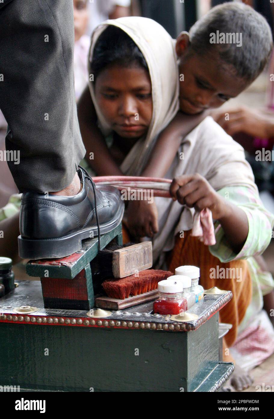 A Bangladeshi boy watches his mother Mazeda Begum, shine the shoes of a ...