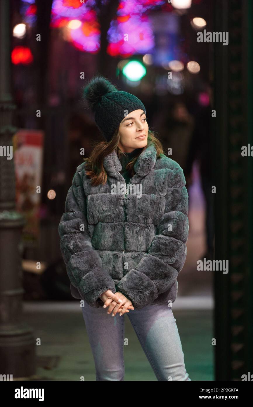 Woman in winter clothes looking in a window of a night store . Winter ...