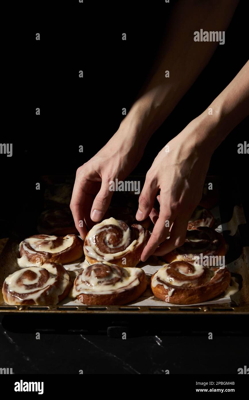 Cinnabon rolls on black background. Hand touches cinnabon from the top ...