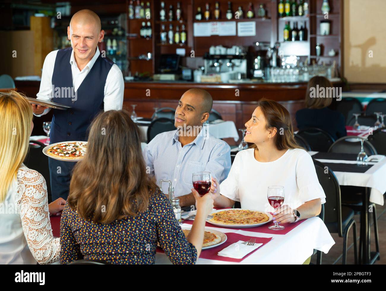 Polite waiter bringing pizza to friends in restaurant Stock Photo - Alamy