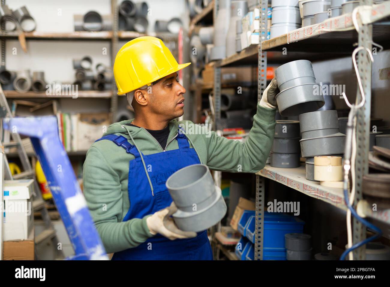 Worker in overalls lays out plumbing fittings on the shelves of ...