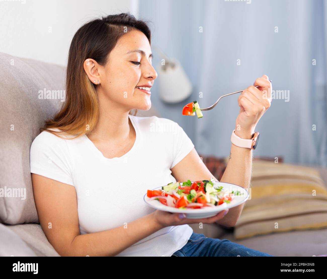 Satisfied woman sitting on sofa at home and eating healthy food Stock ...