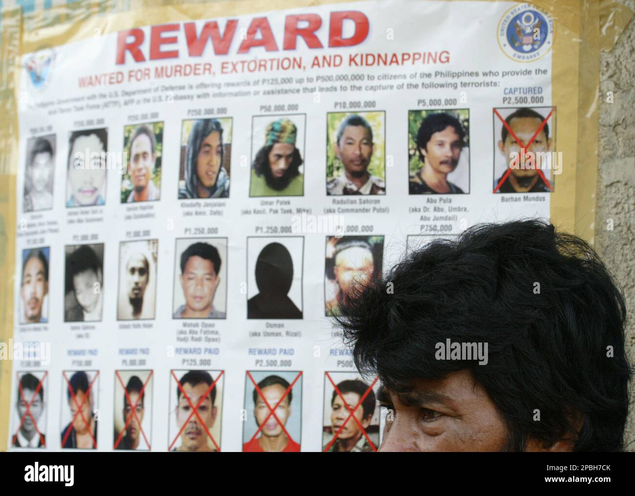 A Filipino Muslim stands next to a wanted poster of 24 Abu Sayyaf ...
