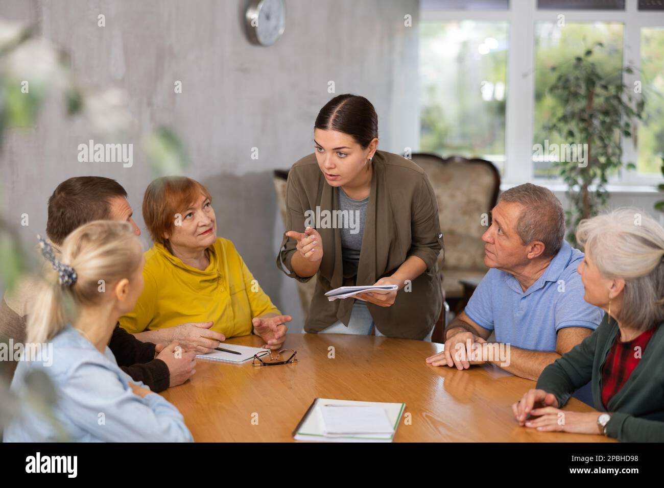 Young female tutor communicating with elderly people in language club ...