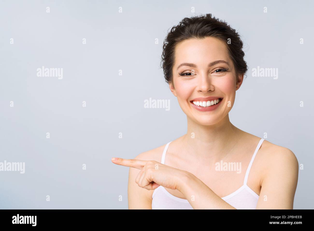 A pretty brunette with a perfect smile points to copyspace. A woman ...