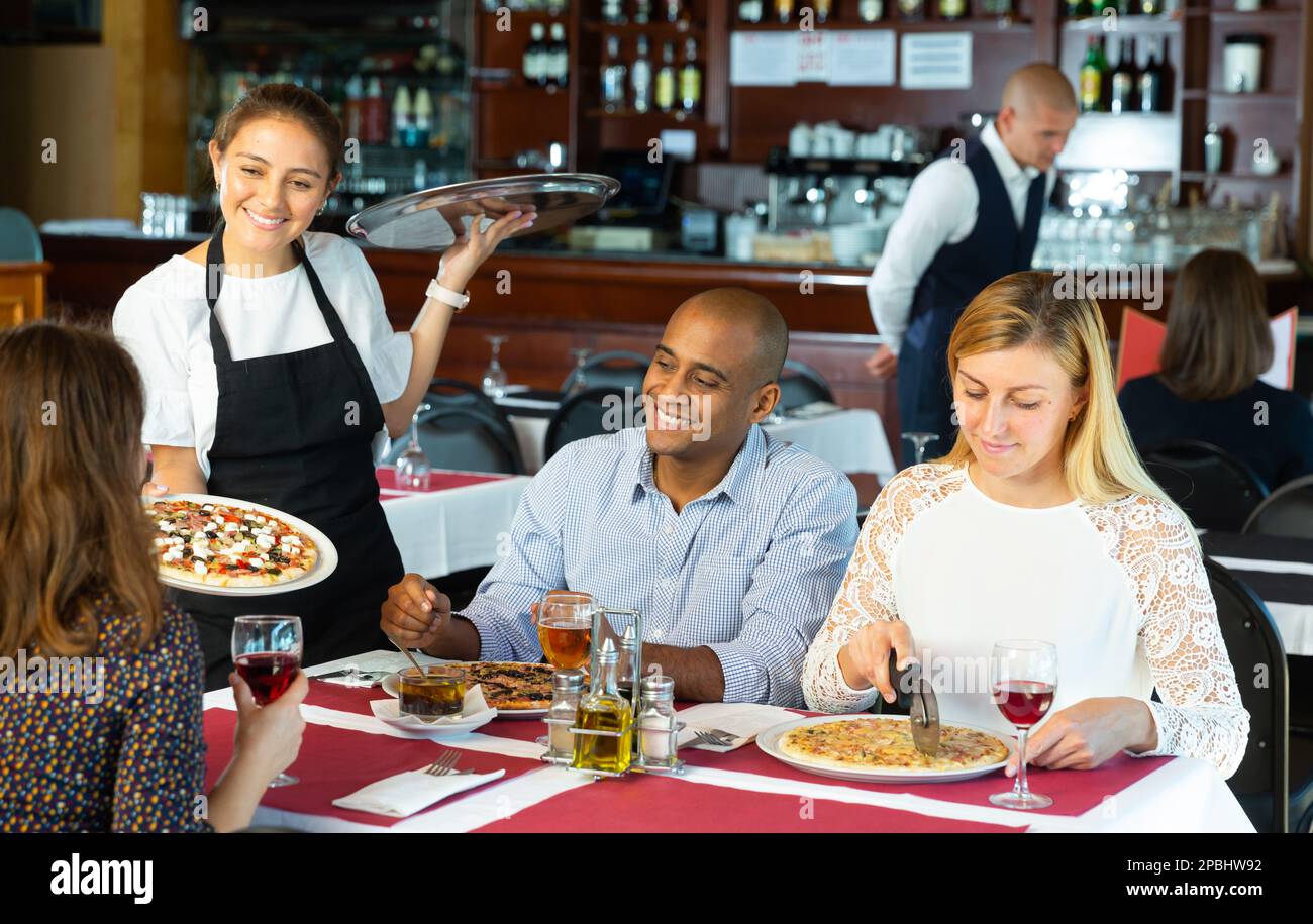 Diligent friendly smiling pleasant waitress with pizza serving man and ...