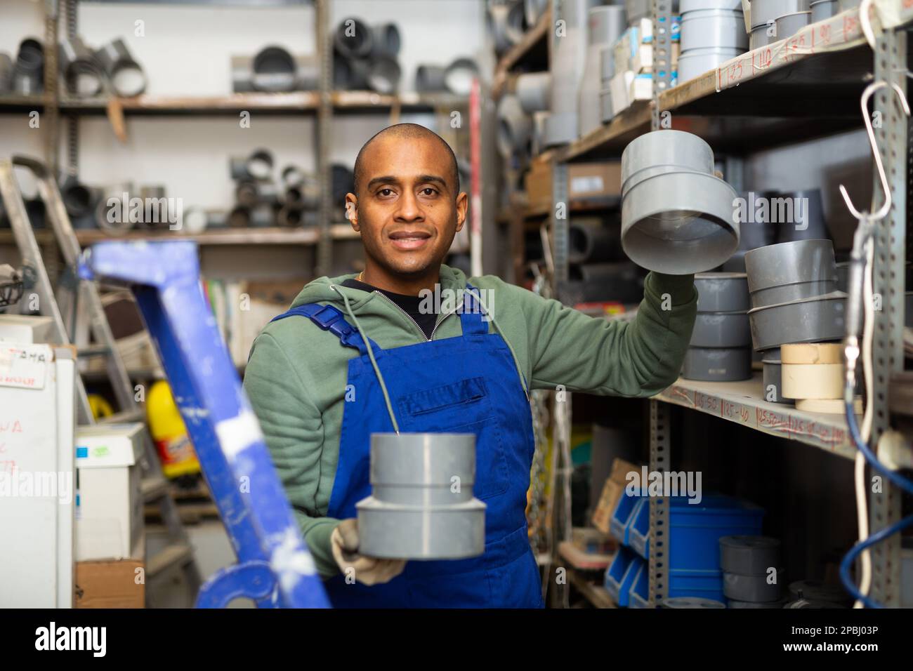 Worker in overalls lays out plumbing fittings on the shelves of ...