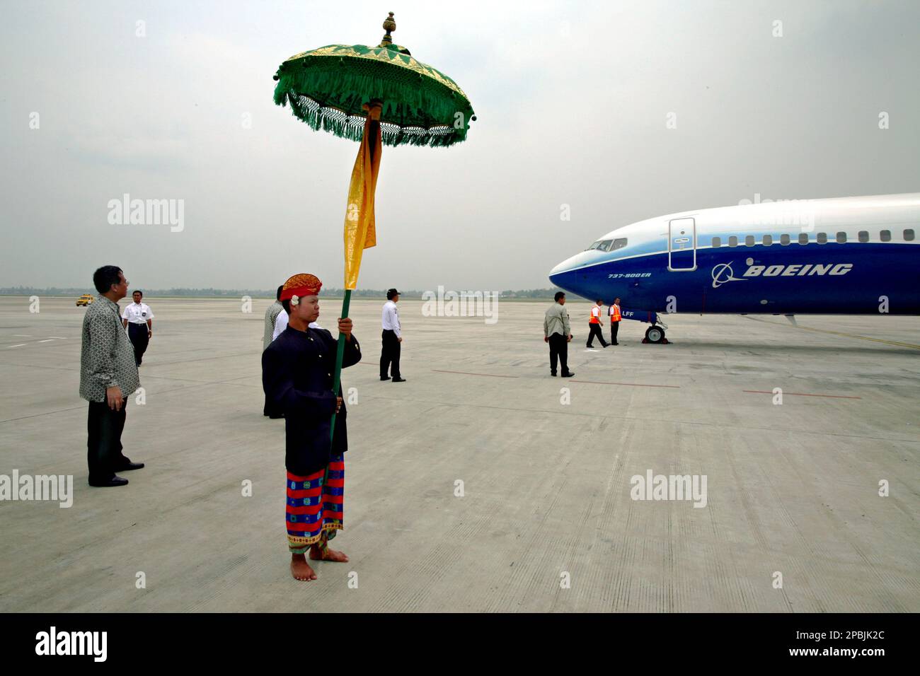 An Indonesian man in a traditional dress stands with a ceremonial ...