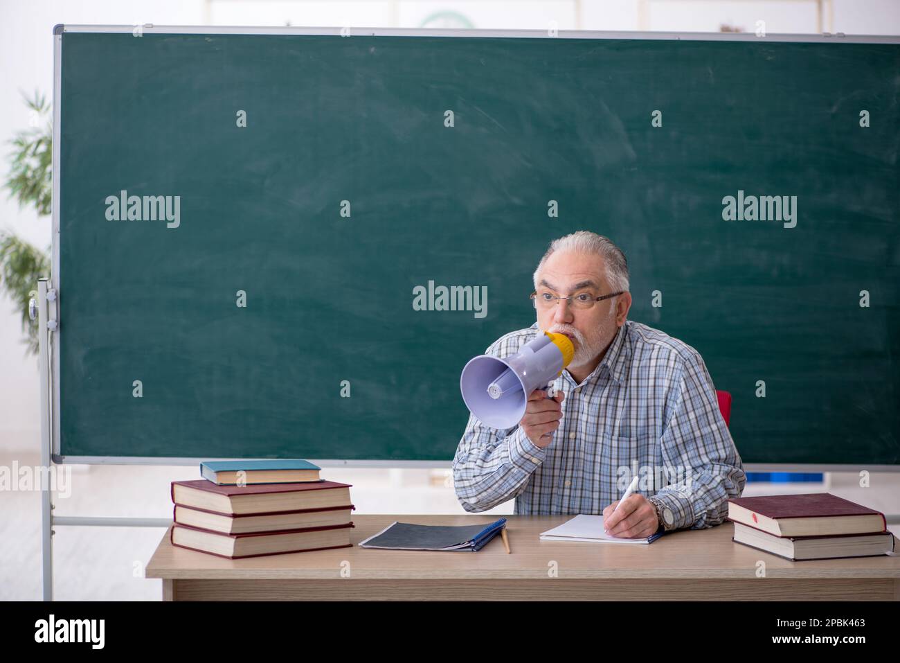 Aged male teacher holding megaphone in the classroom Stock Photo - Alamy