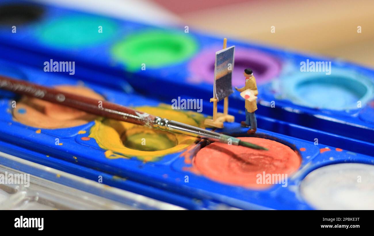 a miniature figure of a painter painting a landscape on watercolors ...