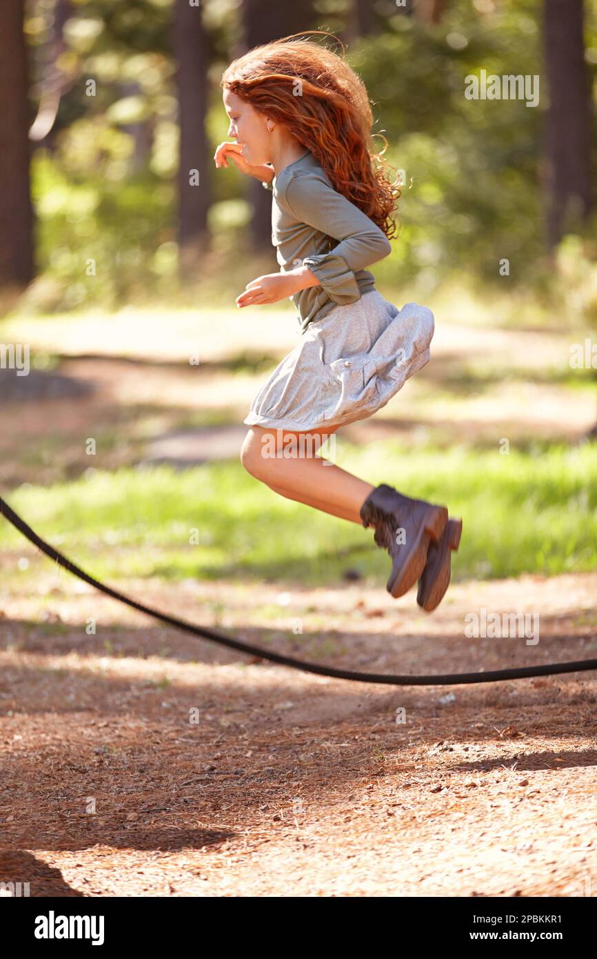 Jumping in happiness. A young red-headed girl jumping over a skipping ...