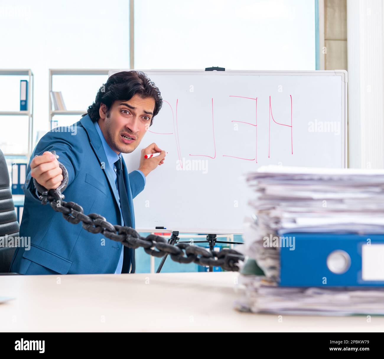 The chained male employee unhappy with excessive work Stock Photo - Alamy