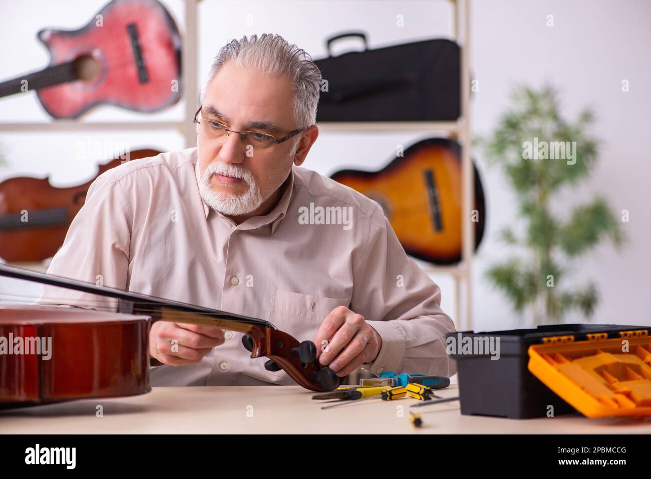 Old repairman repairing musical instruments at workplace Stock Photo ...
