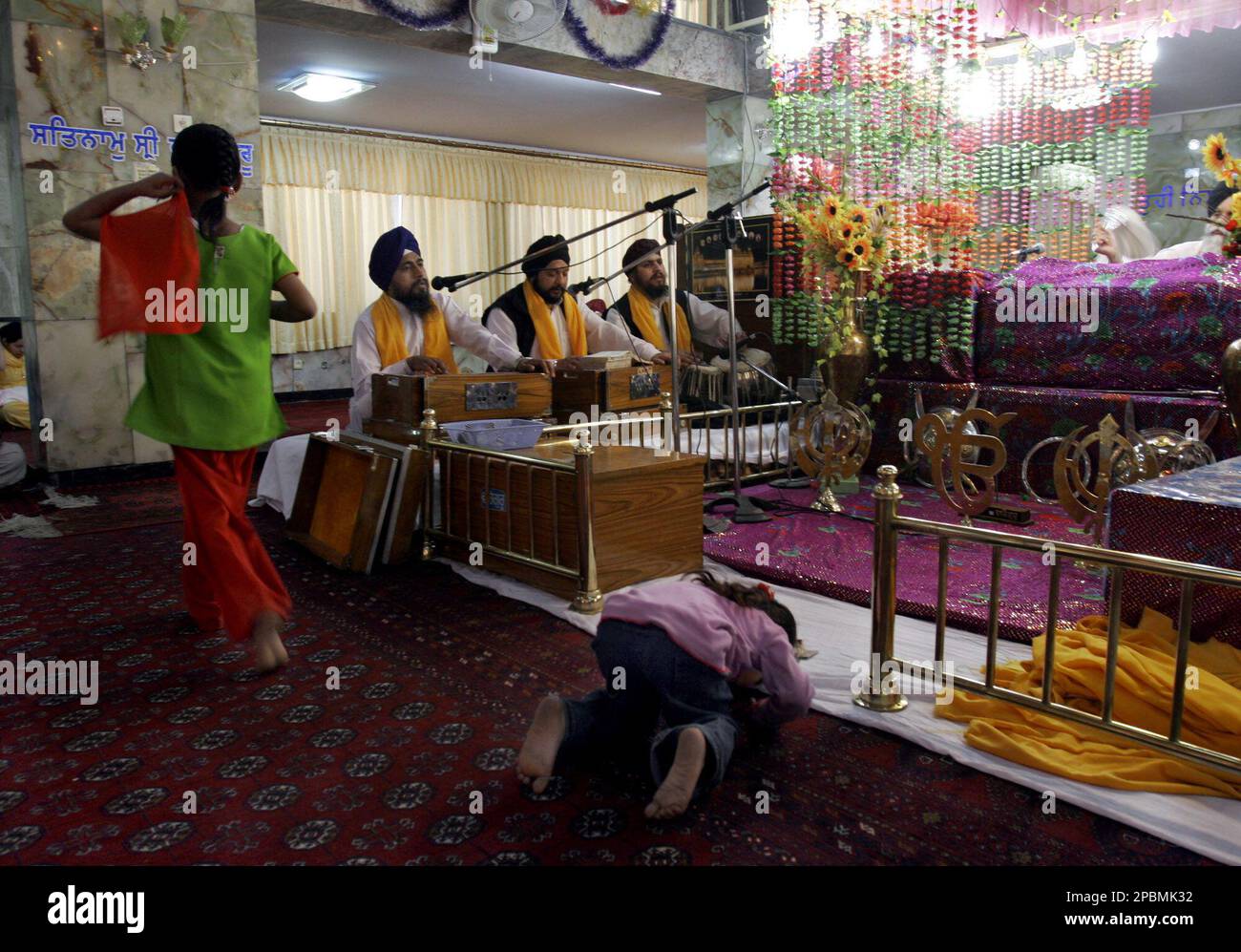 A Sikh devotee girl bows, right, as the Sikh men sing religious songs ...