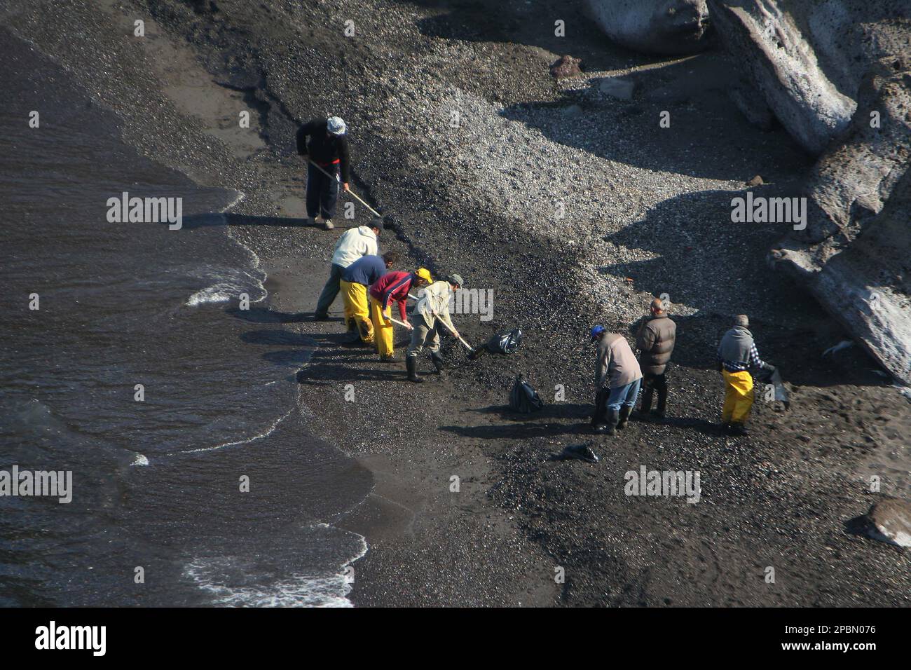 Clean-up crews use shovels to remove oil from a pebble beach on ...