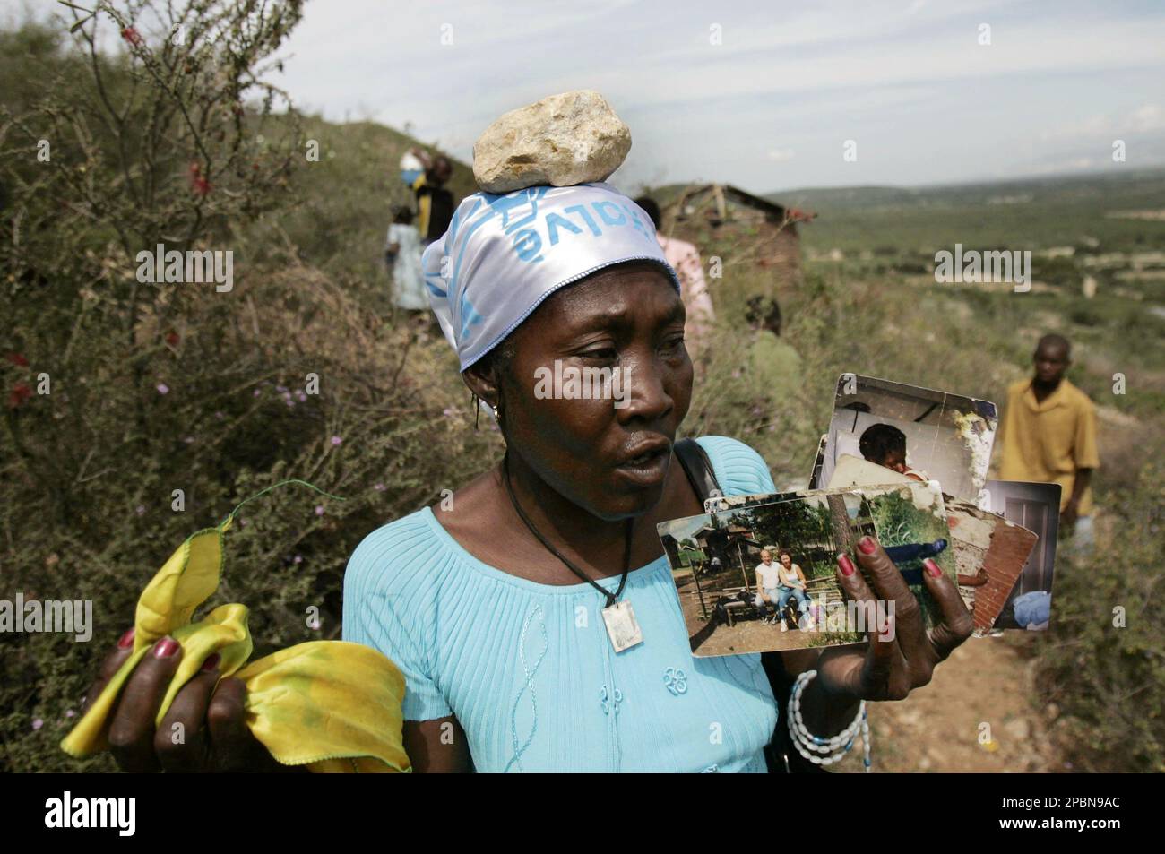 A woman carrying a stone on her head and holding photos of her family ...