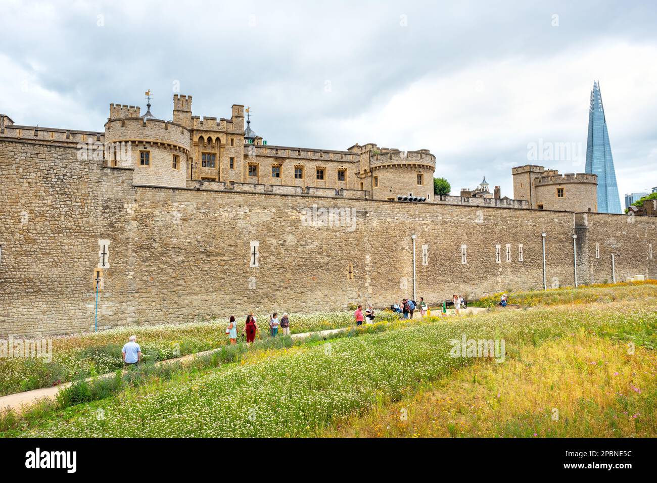 Tourists walk along dry moat around wall of the Tower of London ...