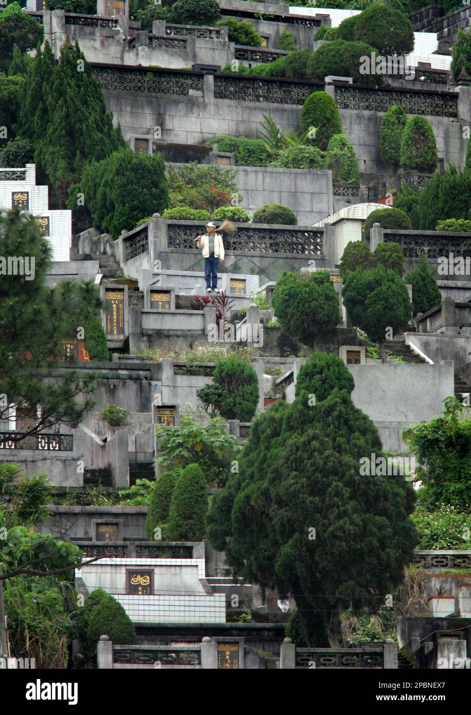 A lone tomb sweeper stands on a hillside of a cemetery during the ...