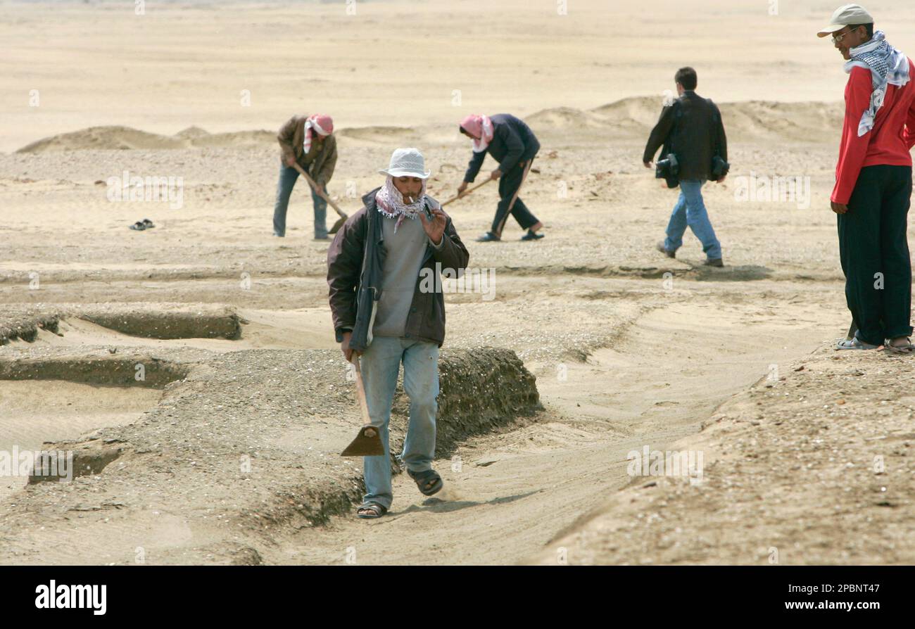 An archaeological worker smokes a cigarette as others remove sand, near ...