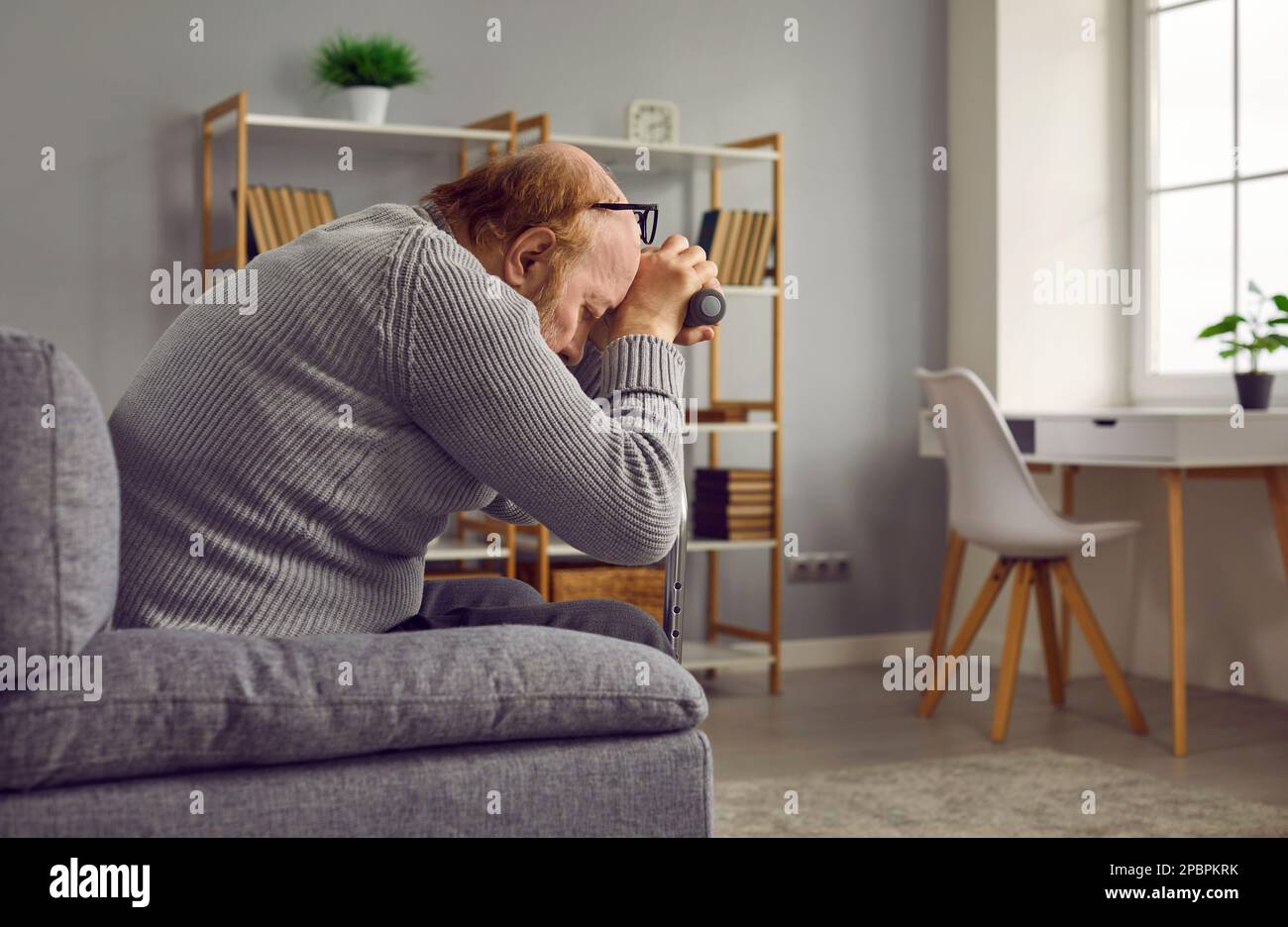 Sad, grieving senior man with a cane is sitting on the couch at home ...