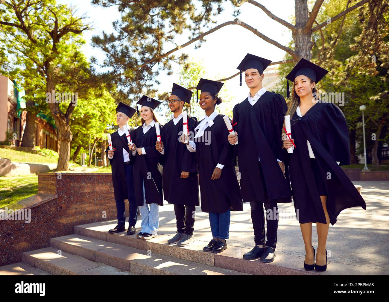 Happy, smart and proud multiracial graduates men and women stand in row ...