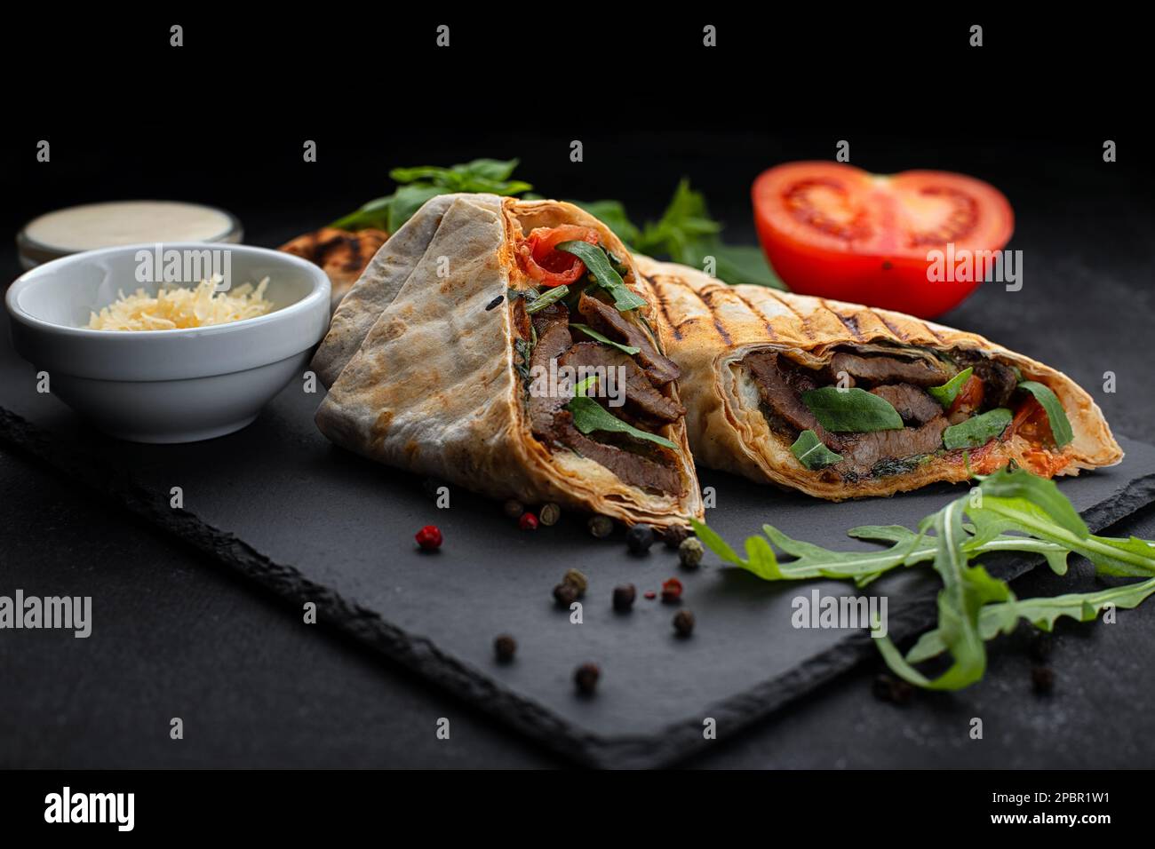 Shawarma with meat, cheese, tomatoes and sauce, on a black background ...