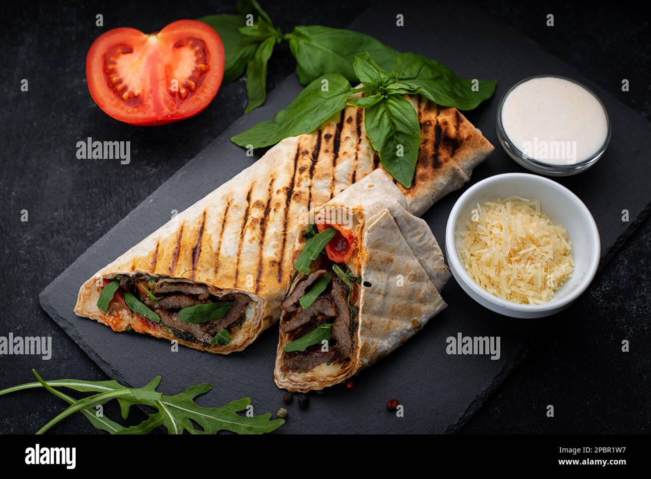 Shawarma with meat, cheese, tomatoes and sauce, on a black background ...