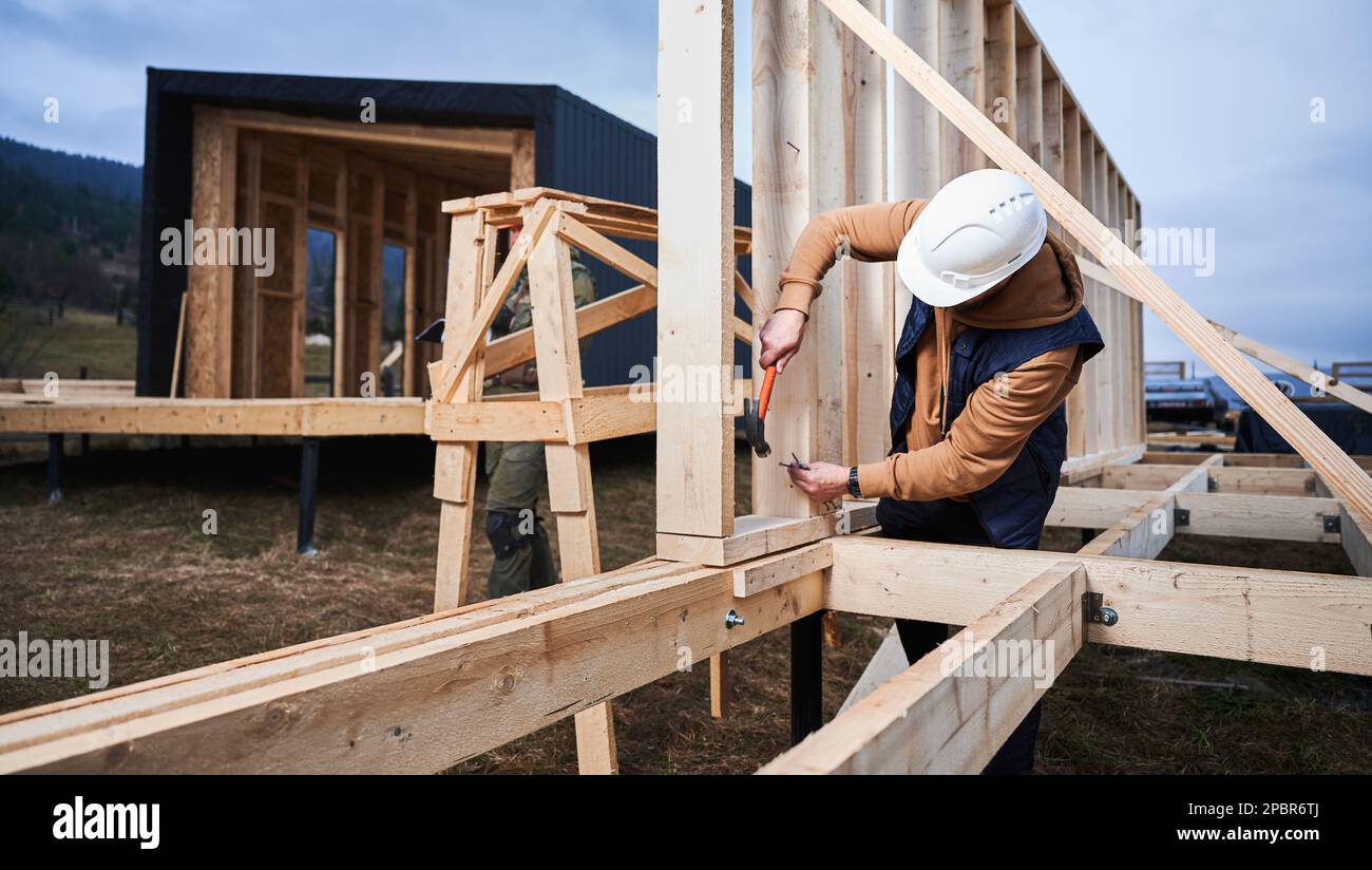 Man worker building wooden frame house on pile foundation. Carpenter ...
