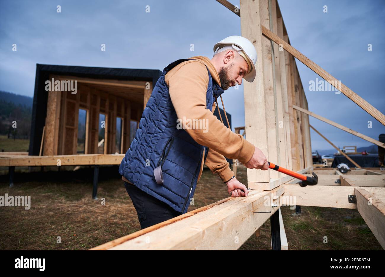 Man worker building wooden frame house on pile foundation. Carpenter ...