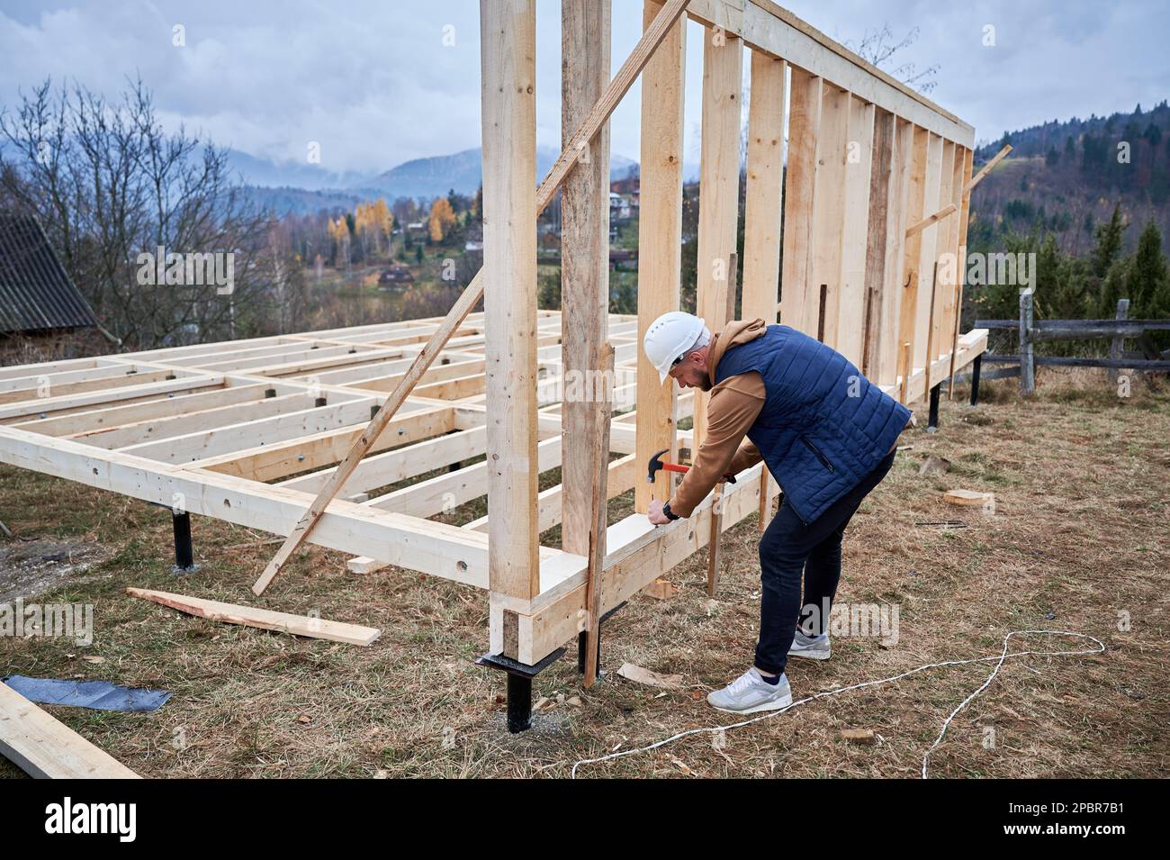 Man worker building wooden frame house on pile foundation. Carpenter ...