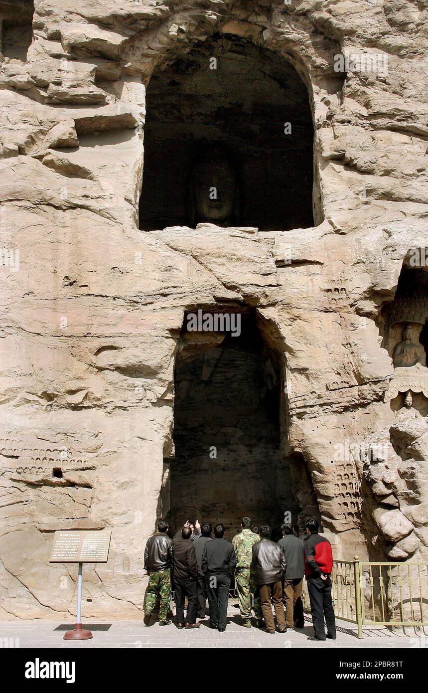 Visitors look at caves at the Yungang Grottoes, ancient Buddhist temple ...