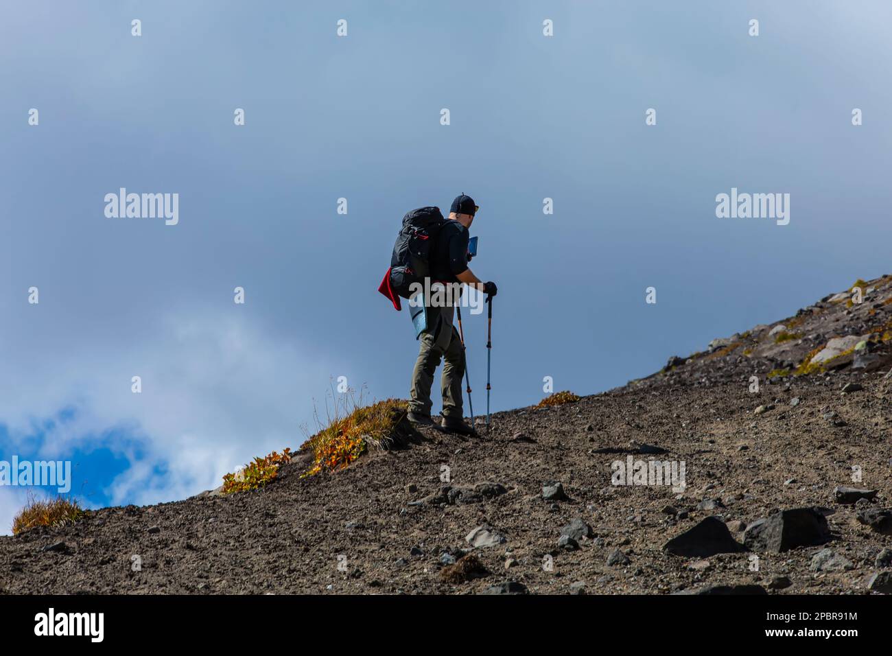 The tourist with a backpack and sticks on the mountain Stock Photo - Alamy